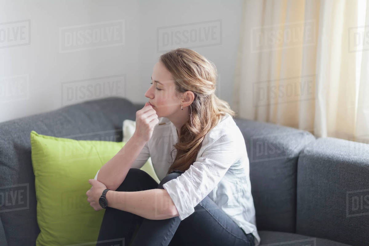 Mid-adult woman sitting on sofa with legs curled up - Royalty-free ...