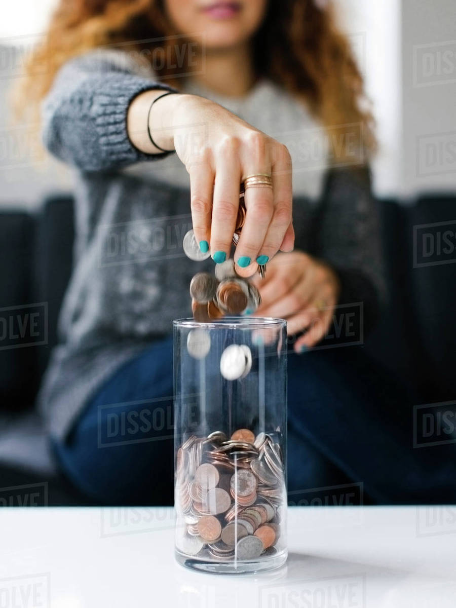 Woman dropping coins into glass container - Royalty-free Stock Photo ...