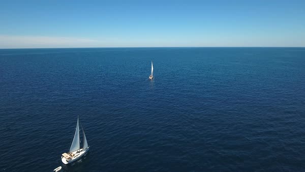 Aerial - Two sail boats sailing on deep blue water to an open sea ...