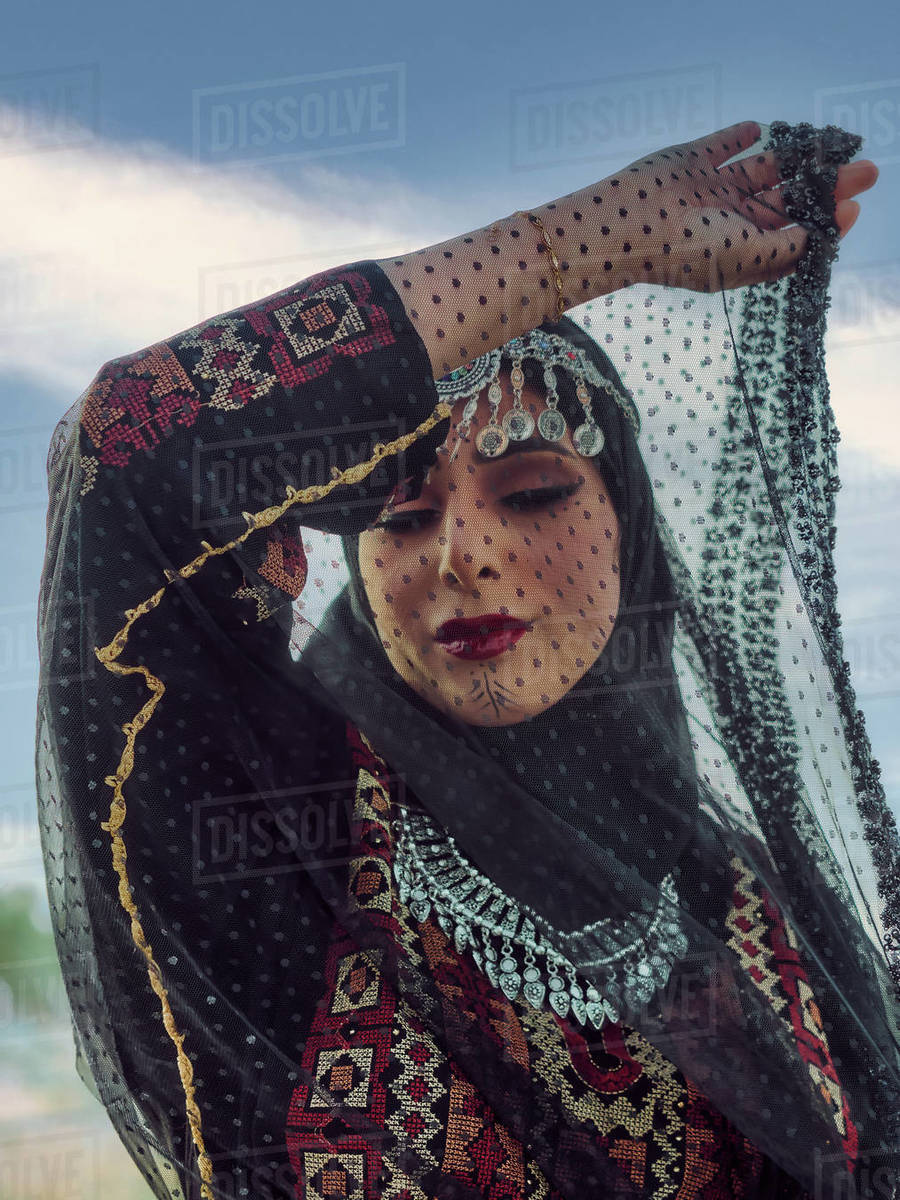 A Saudi girl wearing a hijab and traditional Bedouin attire raises her ...