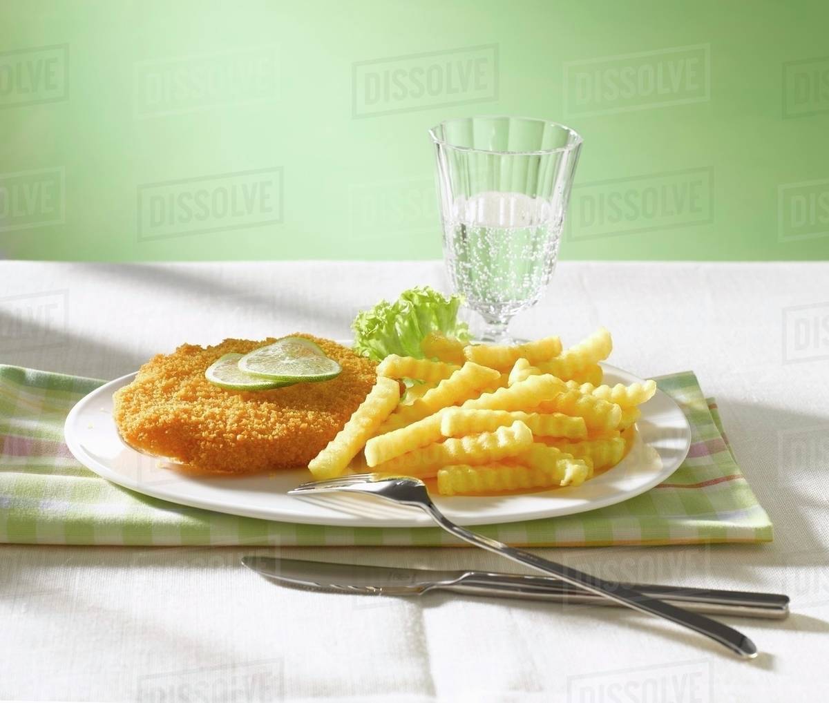 Wiener Schnitzel with lime slices, chips & glass of water - Royalty ...