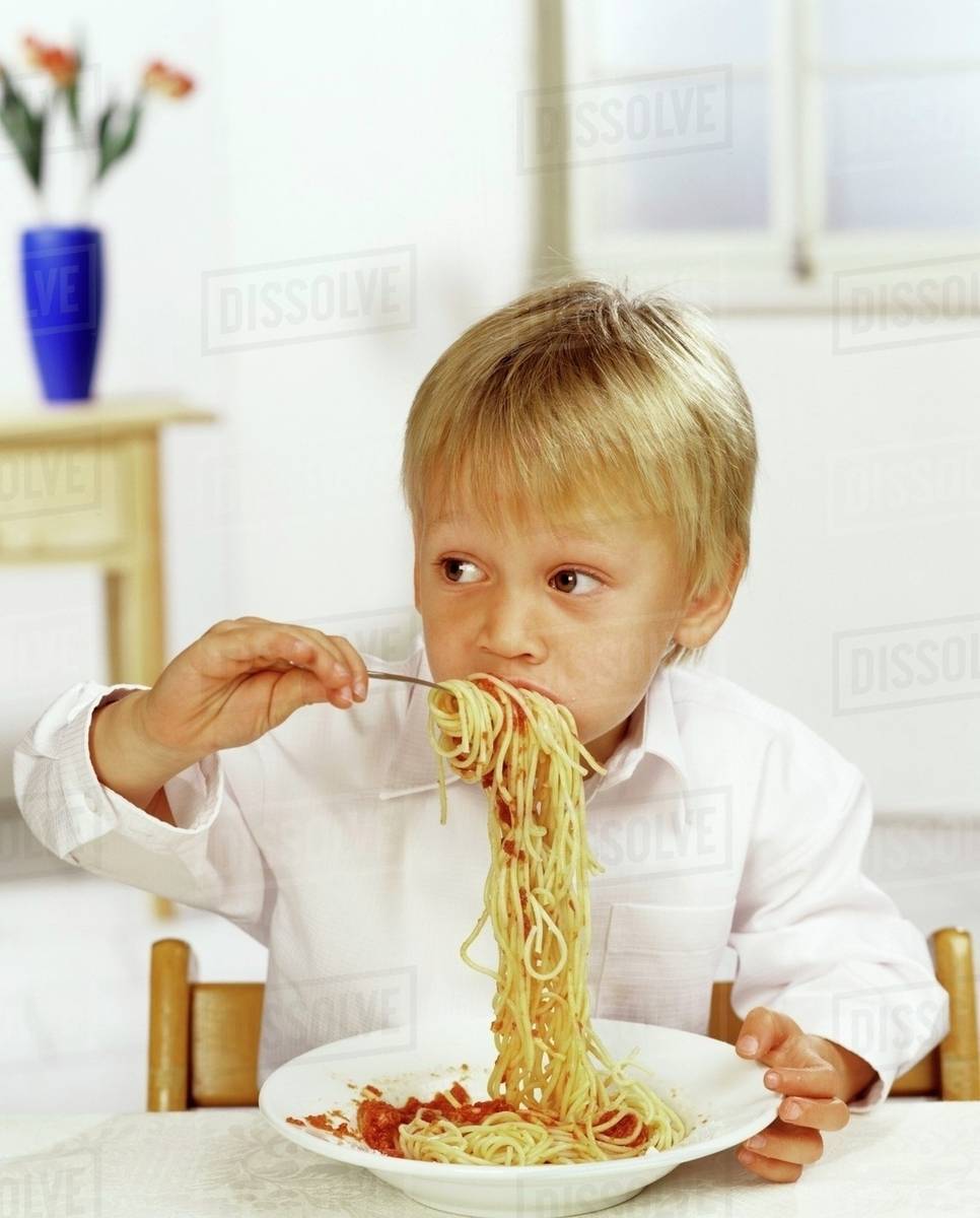 Boy eating spaghetti with tomato sauce - Stock Photo - Dissolve