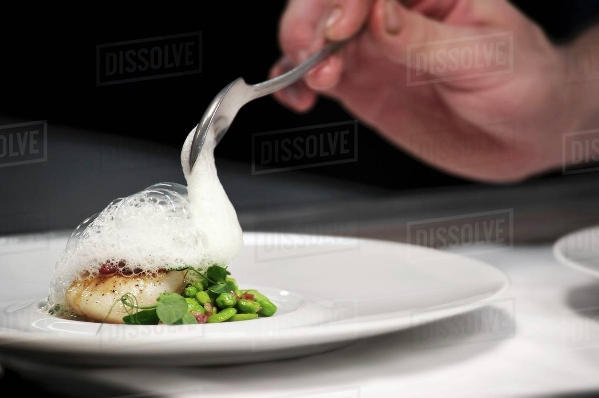 Chef plating up fish and broad bean dish during service at working ...