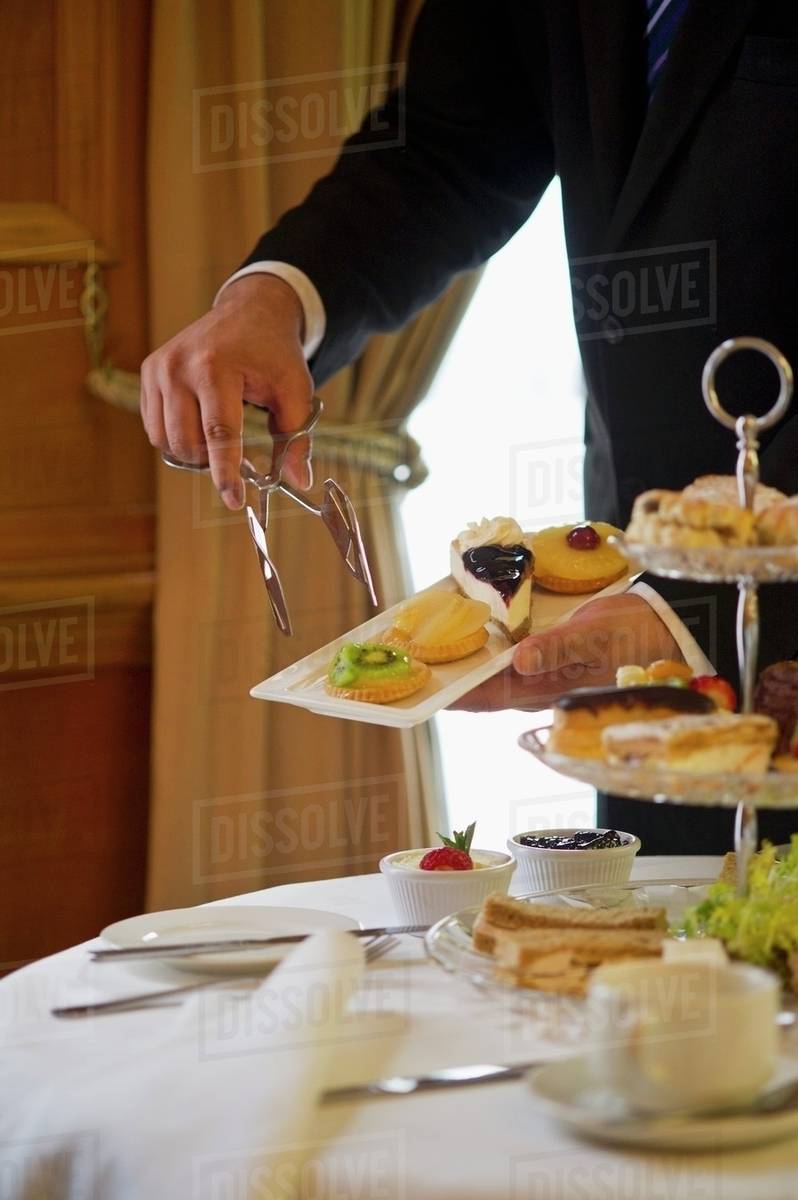 A waiter serving cakes with afternoon tea (England) - Royalty-free ...