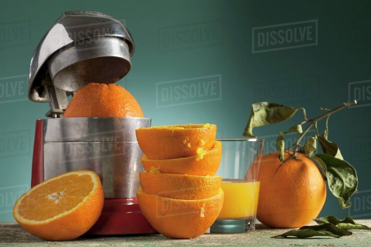 An arrangement of fresh orange juice, an orange press and squeezed ...