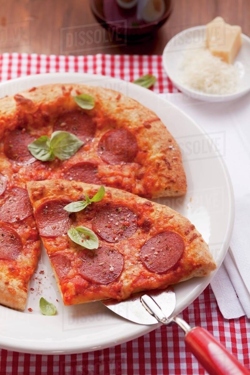 Pizza with salami and basil; one slice of the pizza is on a pizza ...