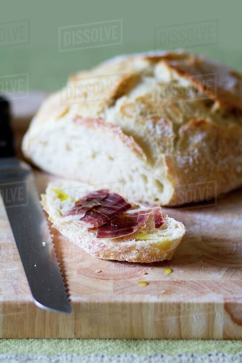 A loaf of bread and a slice of bread topped with cured ham - Stock ...