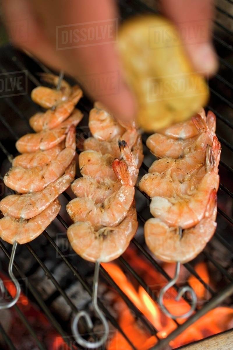 Hand squeezing lemon juice over prawn skewers on grill rack - Royalty ...