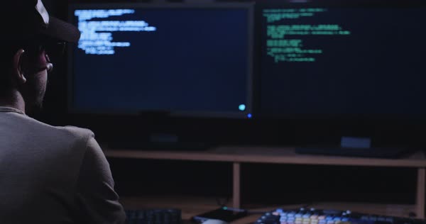 Computer Hacker sitting in a dark room in front of screens and writing ...