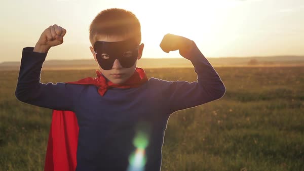 Boy dressed with a Superman cape running in a field, looking into the ...
