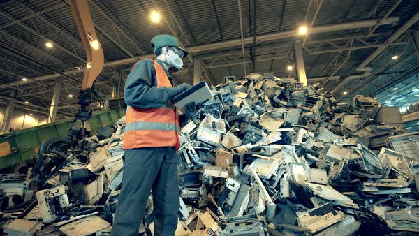 A pile of broken equipment in a dumpsite with a male worker. Garbage ...