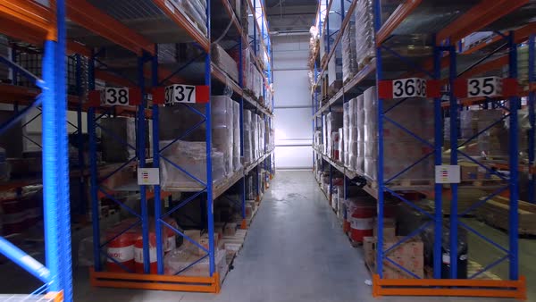 A long dim warehouse corridor with metal racks with empty and full ...