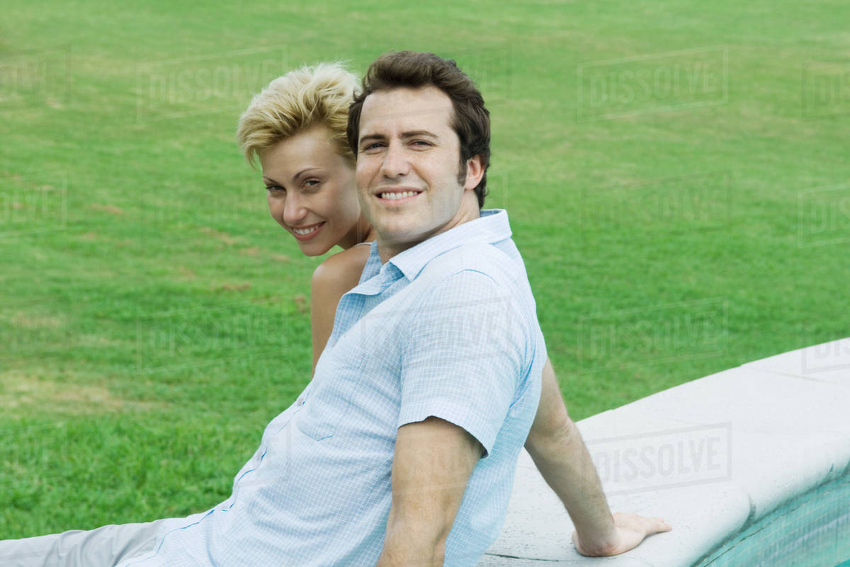 Couple sitting by pool together, smiling at camera - Royalty-free Stock ...