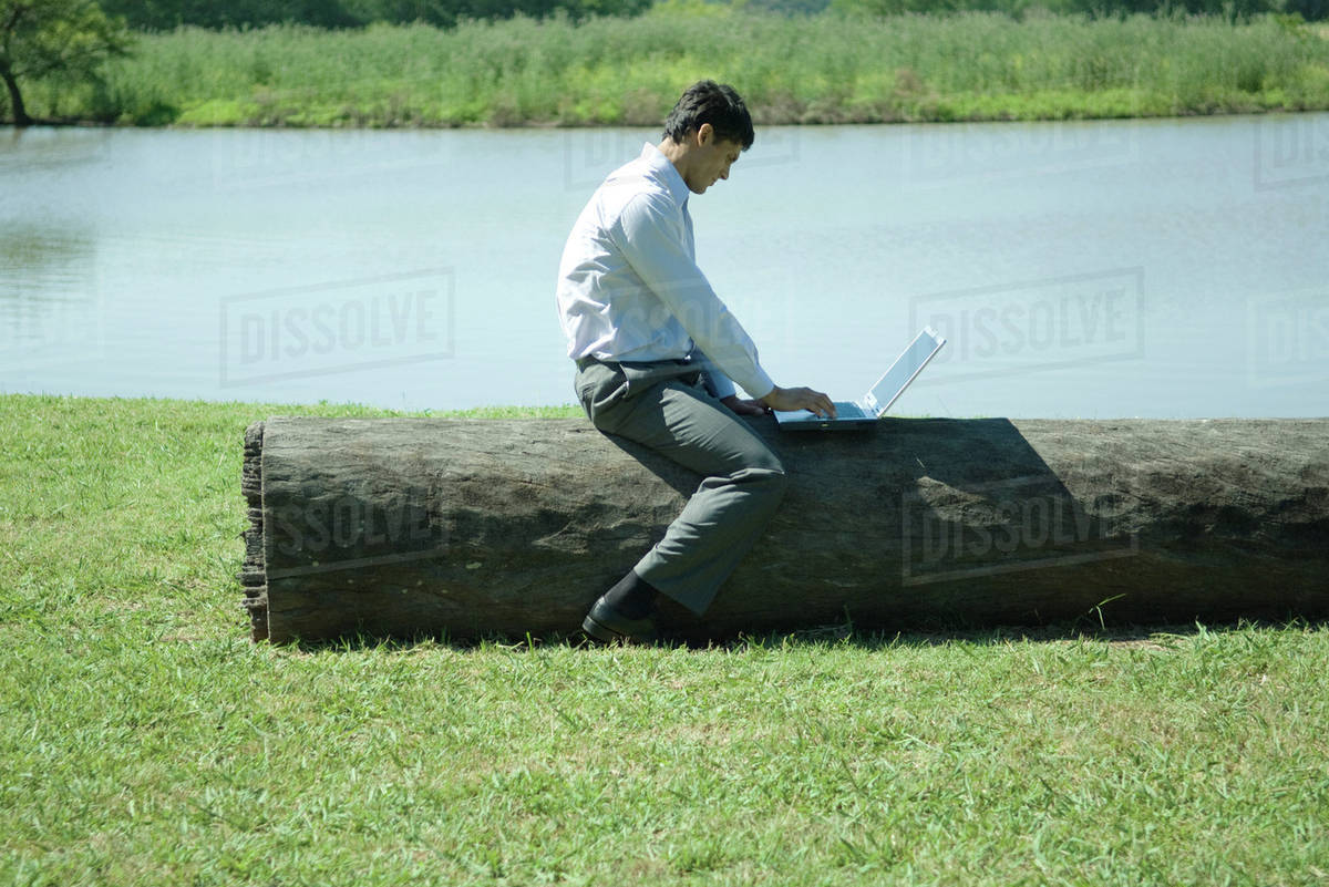 Businessman sitting on log, using laptop - Royalty-free Stock Photo ...