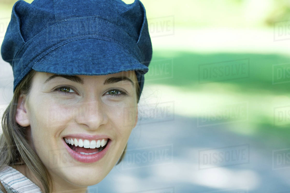 Young woman wearing cap, smiling at camera, portrait - Stock Photo ...