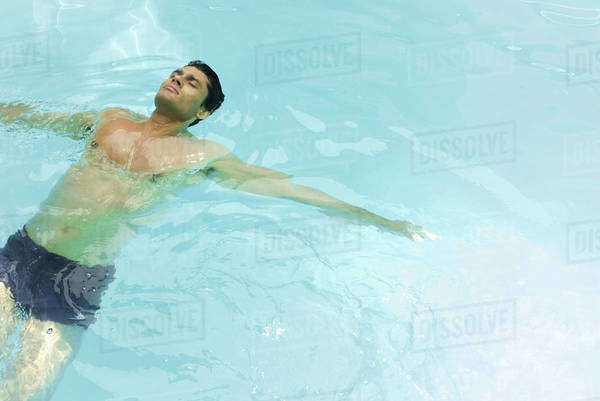 Man floating on back in swimming pool with arms out, eyes closed ...
