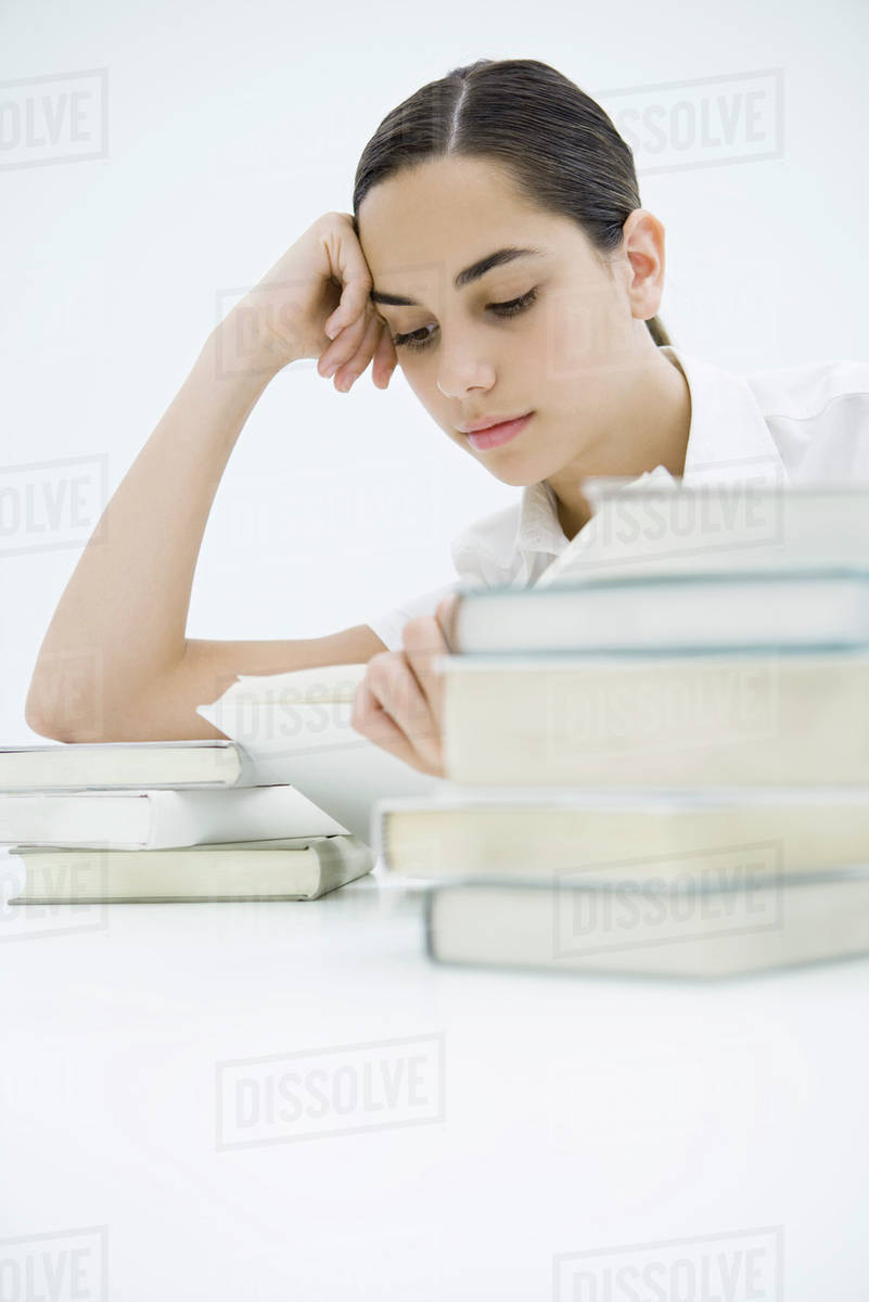 Female reading book, surrounded by two stacks of books, leaning on ...