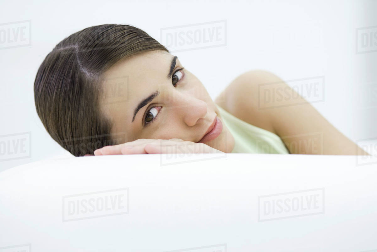 Woman leaning against side of sofa, head resting on hand, smiling at ...