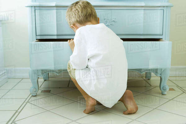 Boy crouching, snooping in chest of drawers - Stock Photo - Dissolve