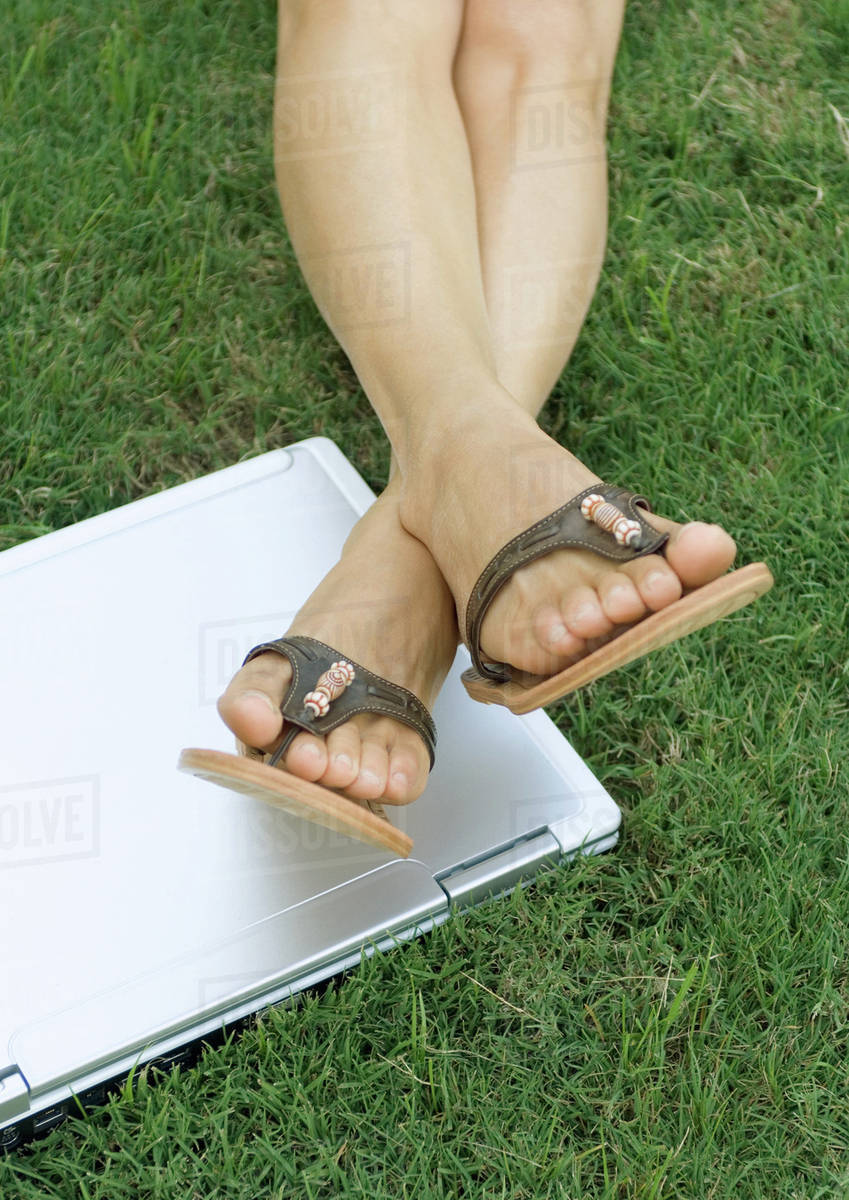 Woman lying in grass, legs resting on laptop computer, low section ...