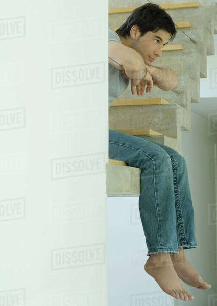 Man sitting on edge of staircase, legs dangling - Stock Photo - Dissolve