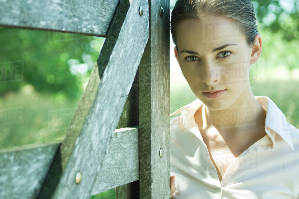Woman standing by wood gate, looking at camera - Stock Photo - Dissolve