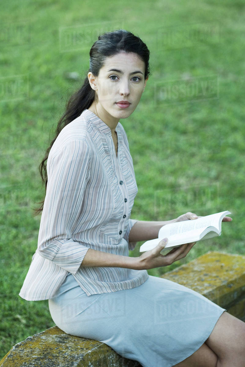 Woman sitting outdoors, reading book, looking up at camera - Royalty ...