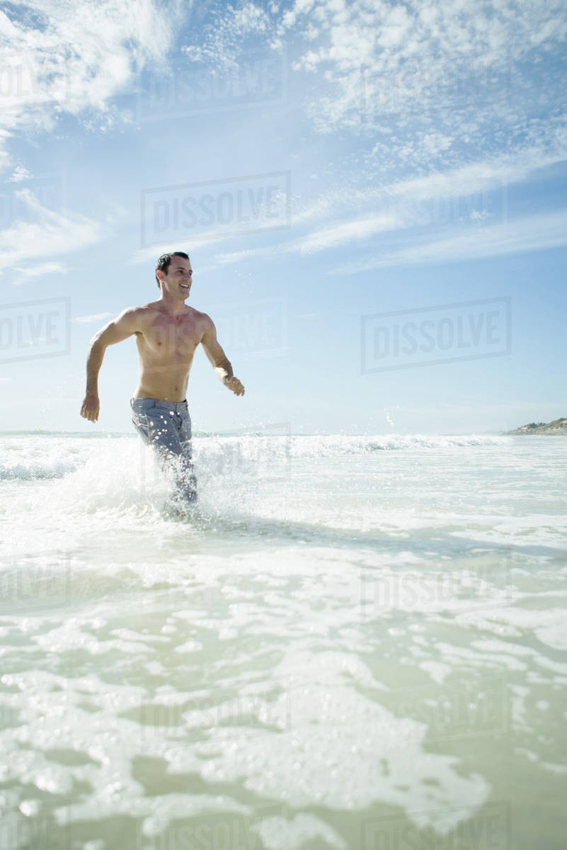 Young man running through surf on beach - Stock Photo - Dissolve