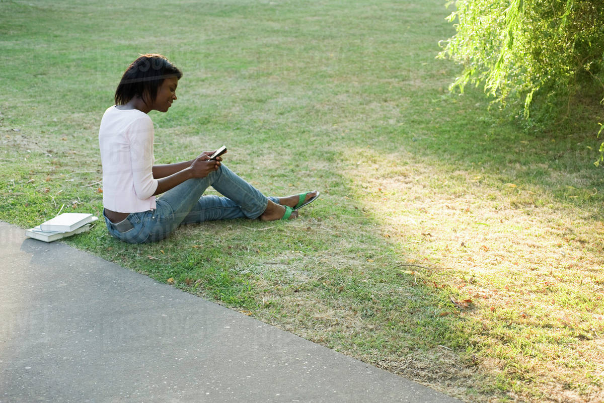 Young woman relaxing in park, text messaging with cell phone - Royalty ...