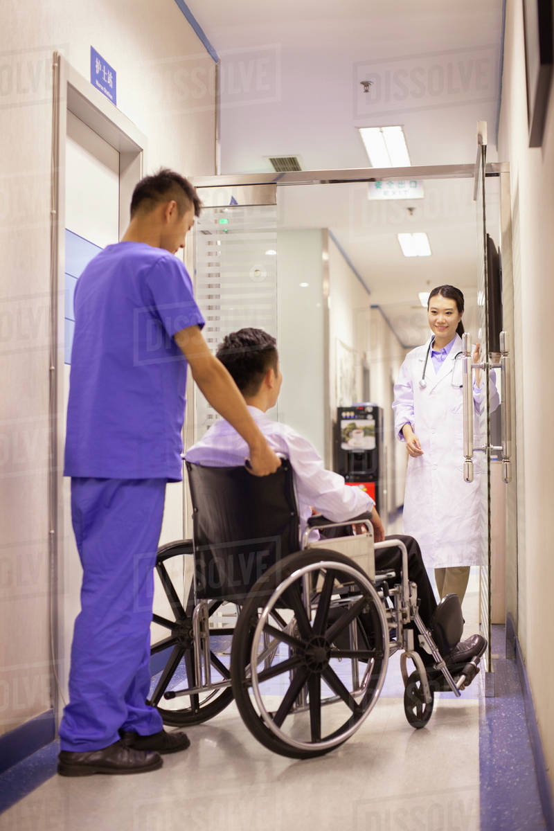 Hospital Staff Pushing Patient In Wheelchair - Stock Photo - Dissolve