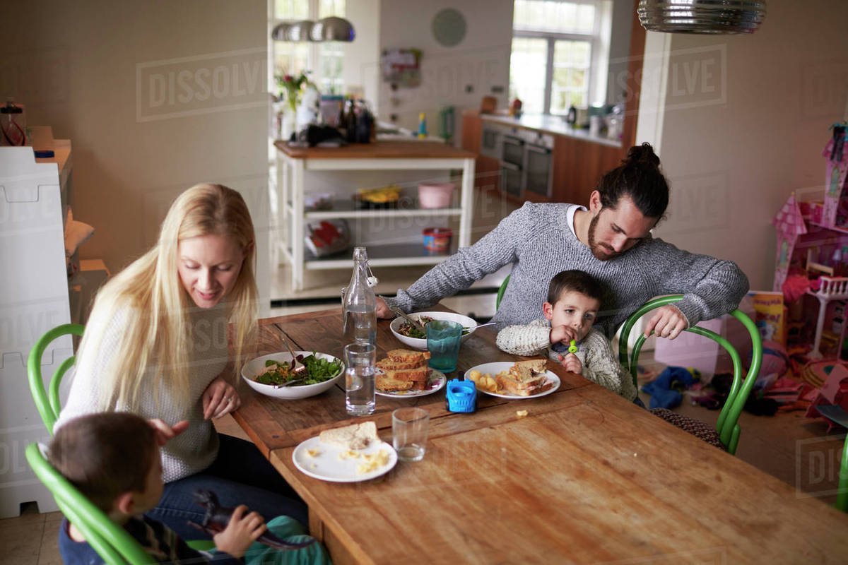 Family sitting at kitchen table and eating meal together - Royalty-free ...
