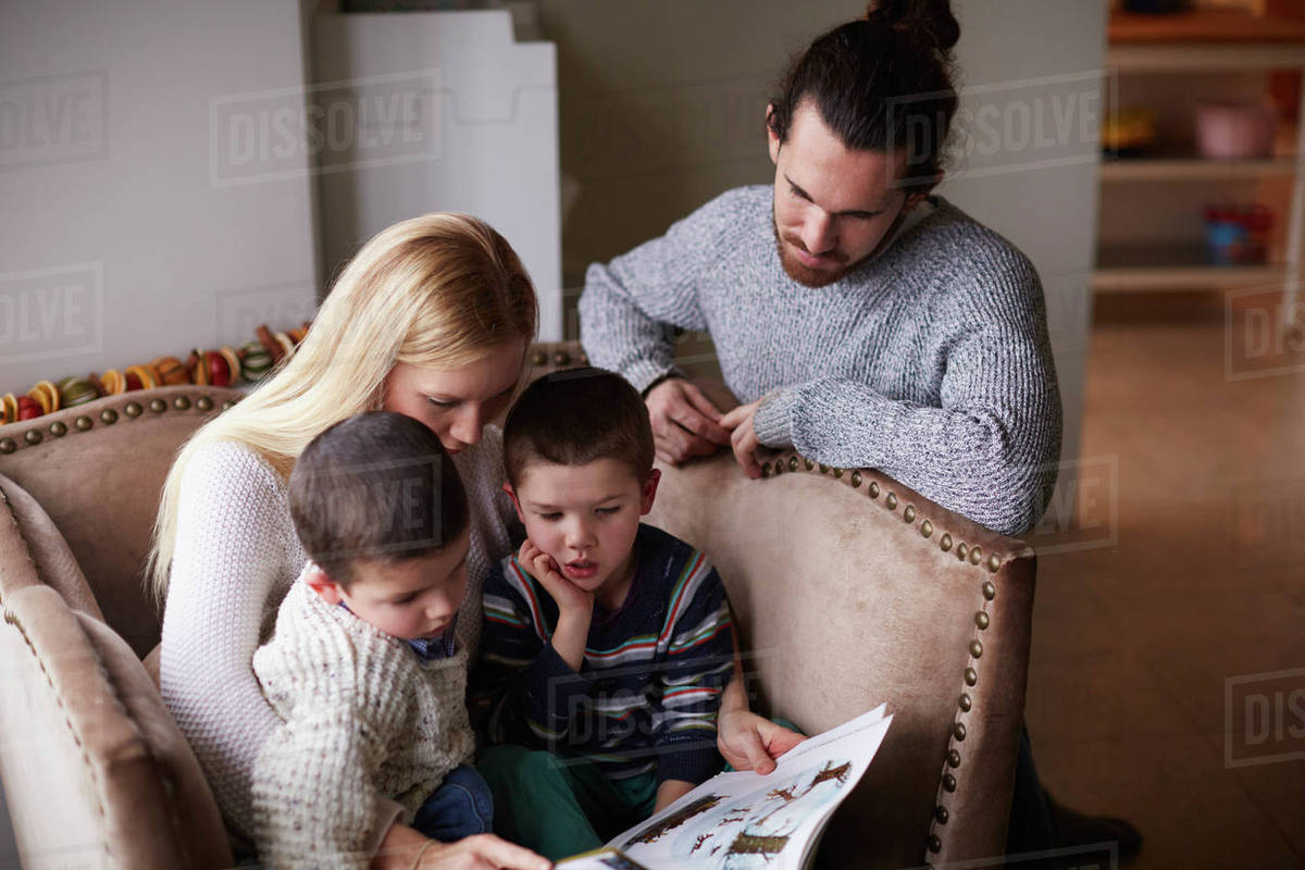 Parents sitting in chair at home reading story to sons - Royalty-free ...