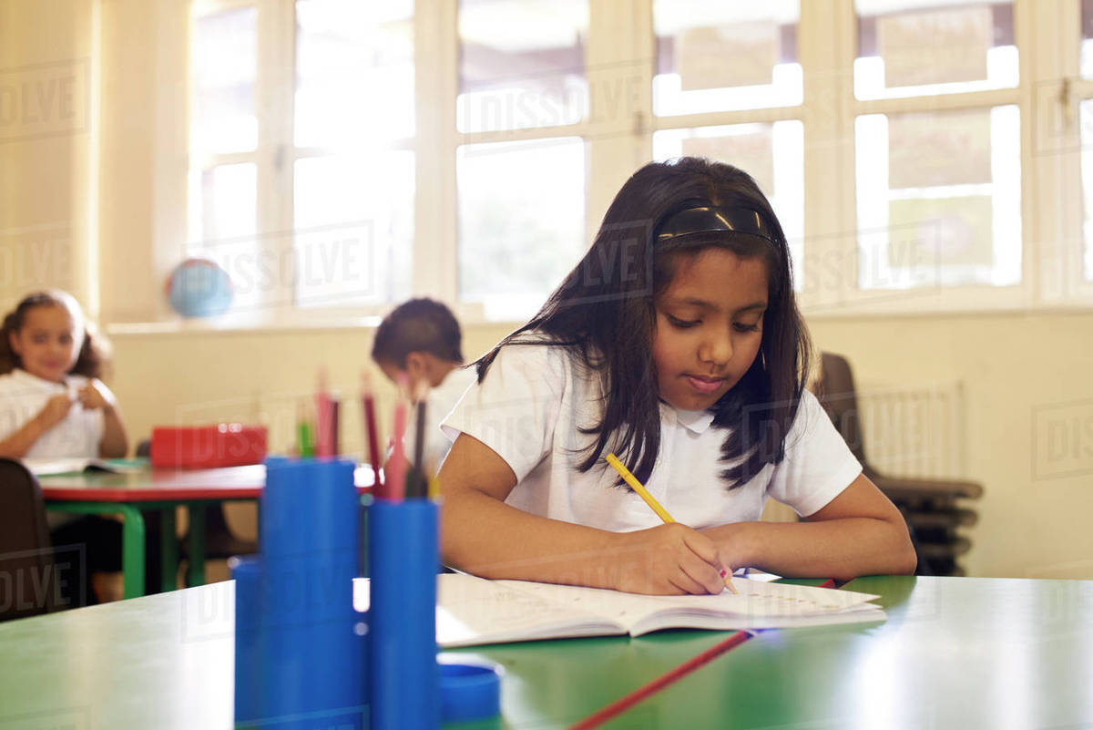 Female pupil working at desk in elementary school classroom - Royalty ...