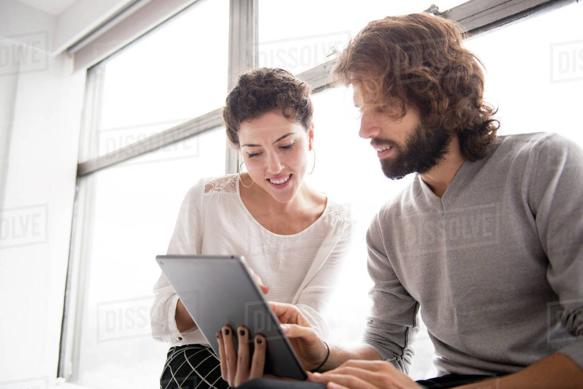 Two colleagues looking at a tablet computer by a window in a high rise ...