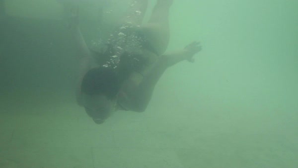 Young woman swimming underwater in pool and then emerging to smile at ...