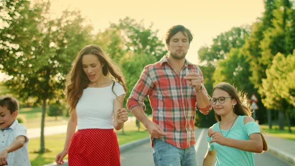 Positive parents and kids walking on street. Happy family dancing ...