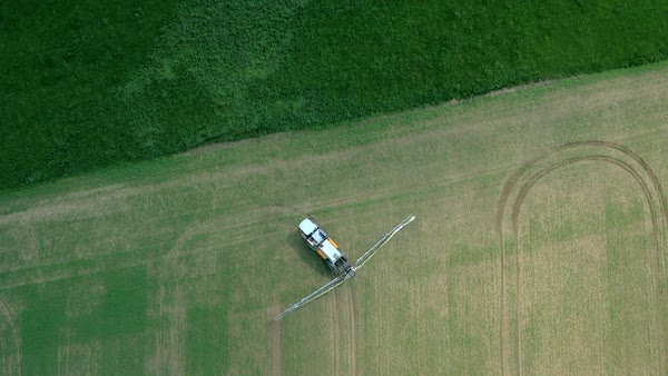 Aerial tracking shot of tractor spreading pesticides in field, bird's ...