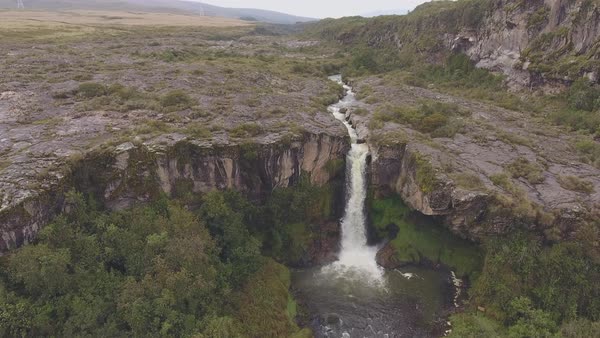 Aerial tracking shot of a waterfall flowing over an old andesitic lava ...