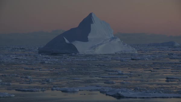 Tracking shot through pack ice, around a pyramid-shaped iceberg ...