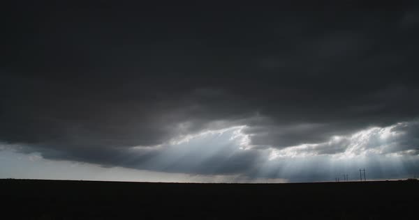 Slow pan right, white sunbeams shine down through dark clouds, rural ...