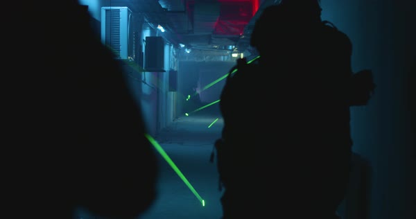 Back view of anonymous SWAT team with laser sights walking in dark ...