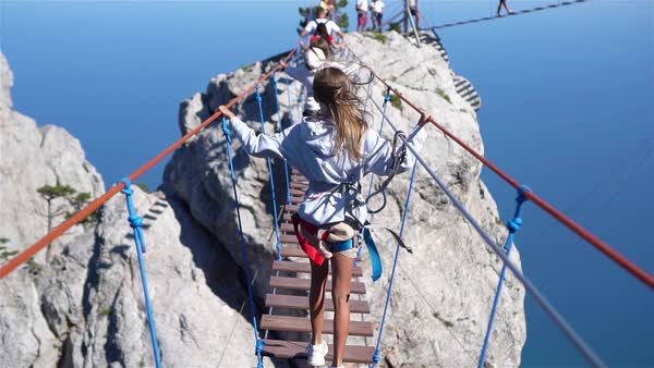 Girls crossing the chasm on the rope bridge. Black sea background ...