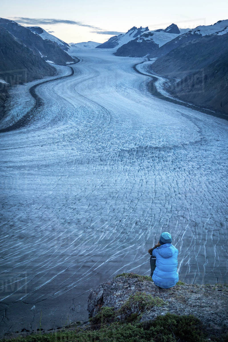 Rear view of a woman looking at view while sitting on rock, Alaska ...