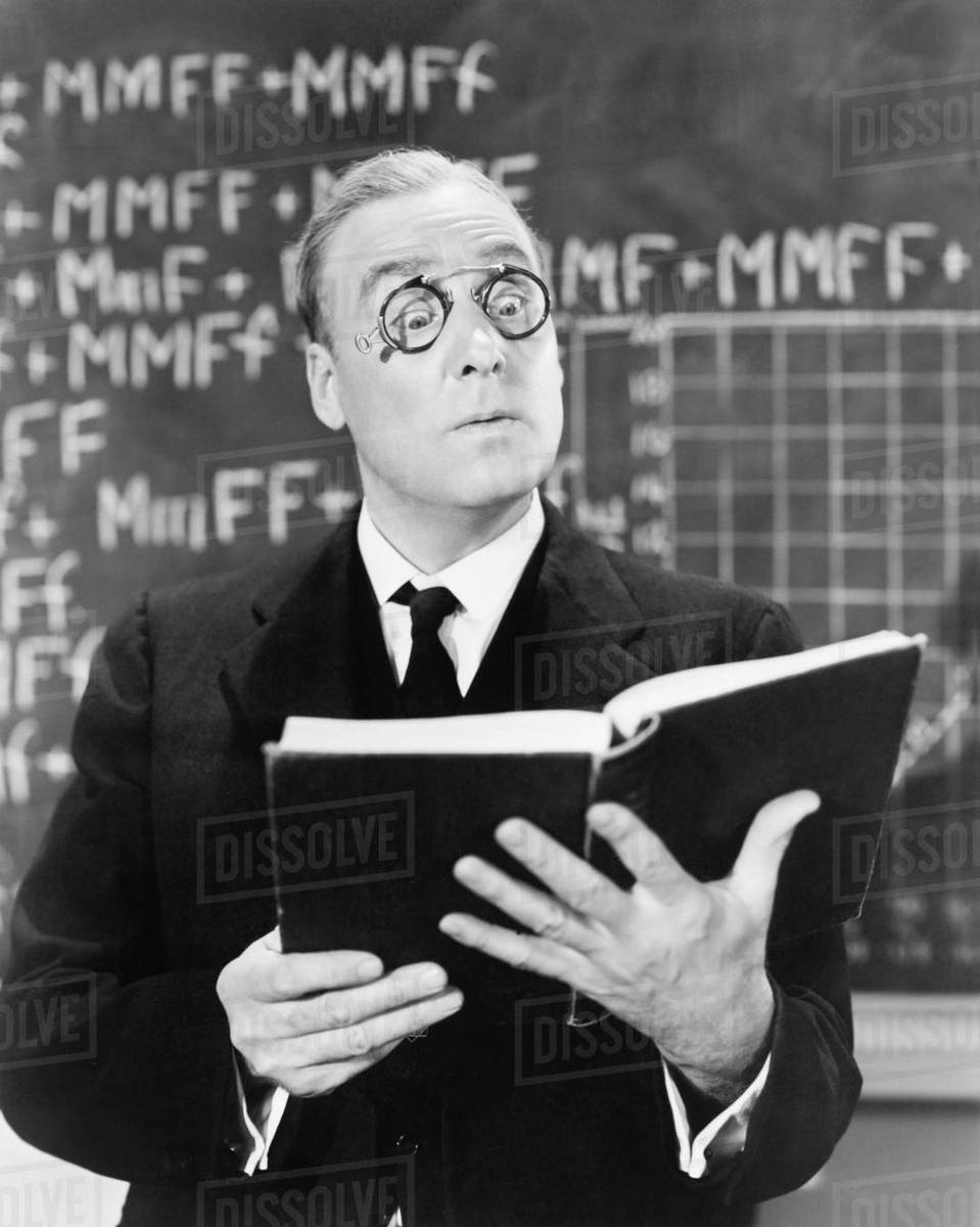 Teacher holding a book in front of a black board looking surprised ...