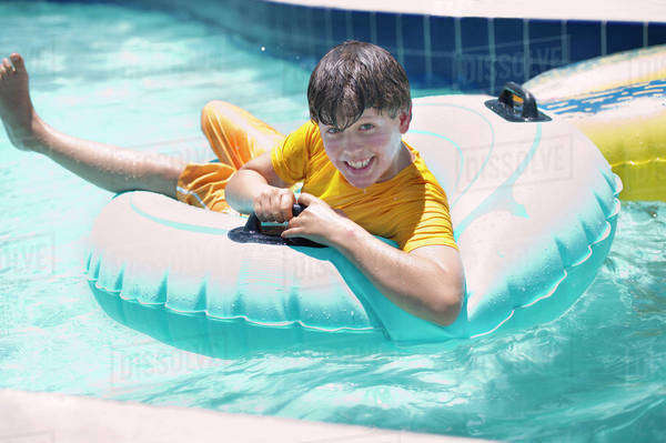 Hispanic boy floating on raft in swimming pool - Stock Photo - Dissolve