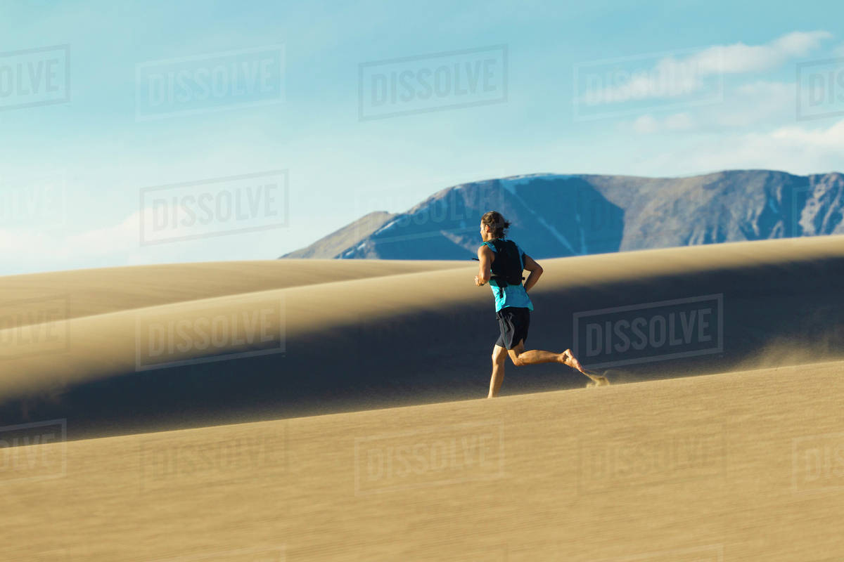 Hispanic man running on sand dune - Royalty-free Stock Photo | Dissolve