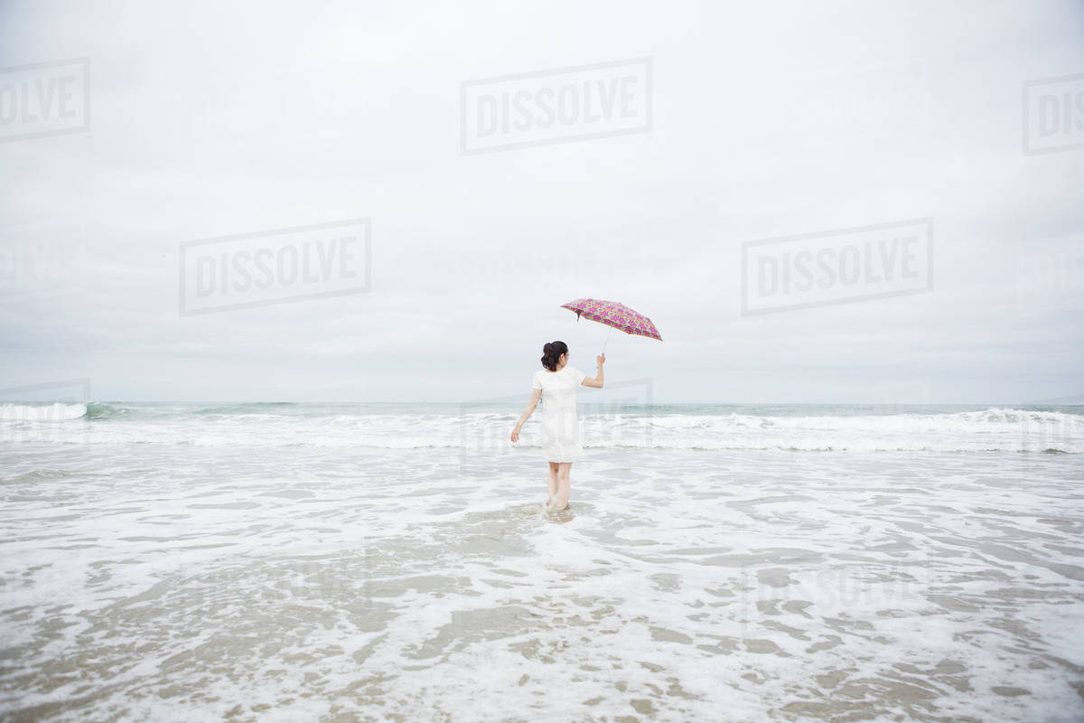 Woman wading with umbrella on beach - Royalty-free Stock Photo | Dissolve