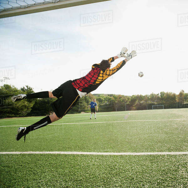 Mixed race goalkeeper in mid-air protecting goal - Royalty-free Stock ...