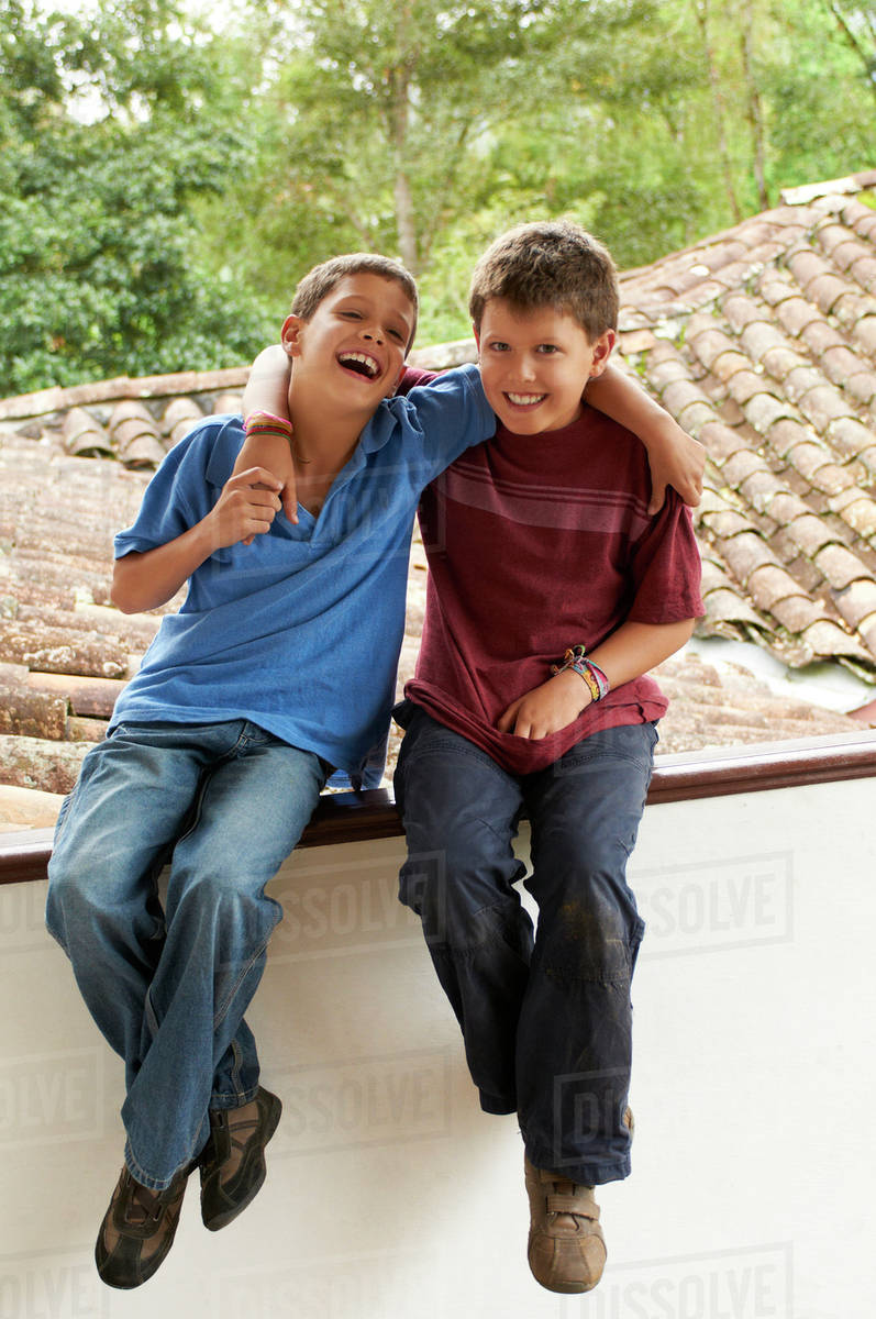 Hispanic boys sitting on roof hugging - Stock Photo - Dissolve