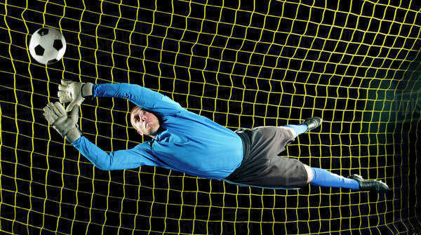 Caucasian soccer goalie jumping in mid-air catching ball at night ...